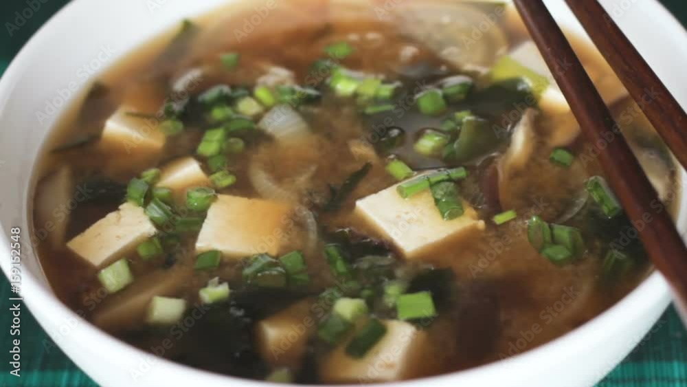 Extreme close up of sprinkling big bowl of miso soup with diced green ...