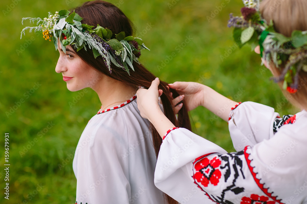 Midsummer. Two girls in the Slavic clothes weave braids in the hair ...