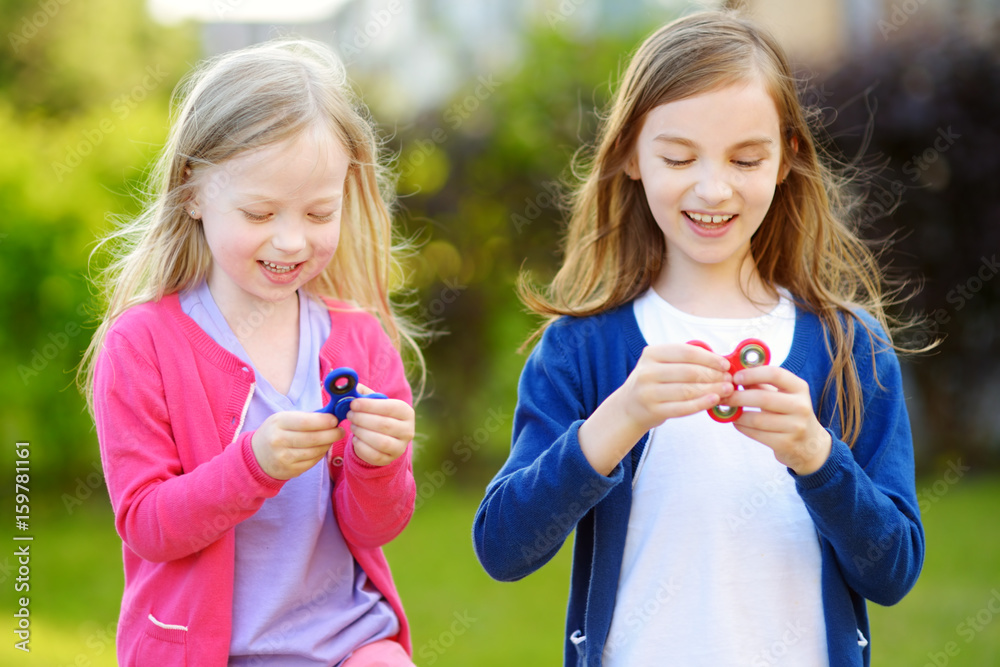 Two funny sisters playing with fidget spinners on the playground ...