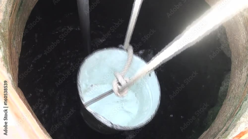 A person is drawing water from a well using a rope with a pulley and a ...