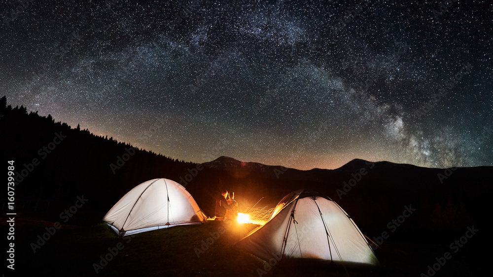 Night camping. Couple tourists sitting and hugging at a campfire near ...
