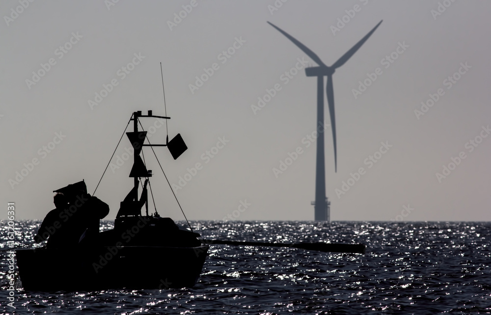 Sustainable resources. Small fishing boat infront of offshore wind ...