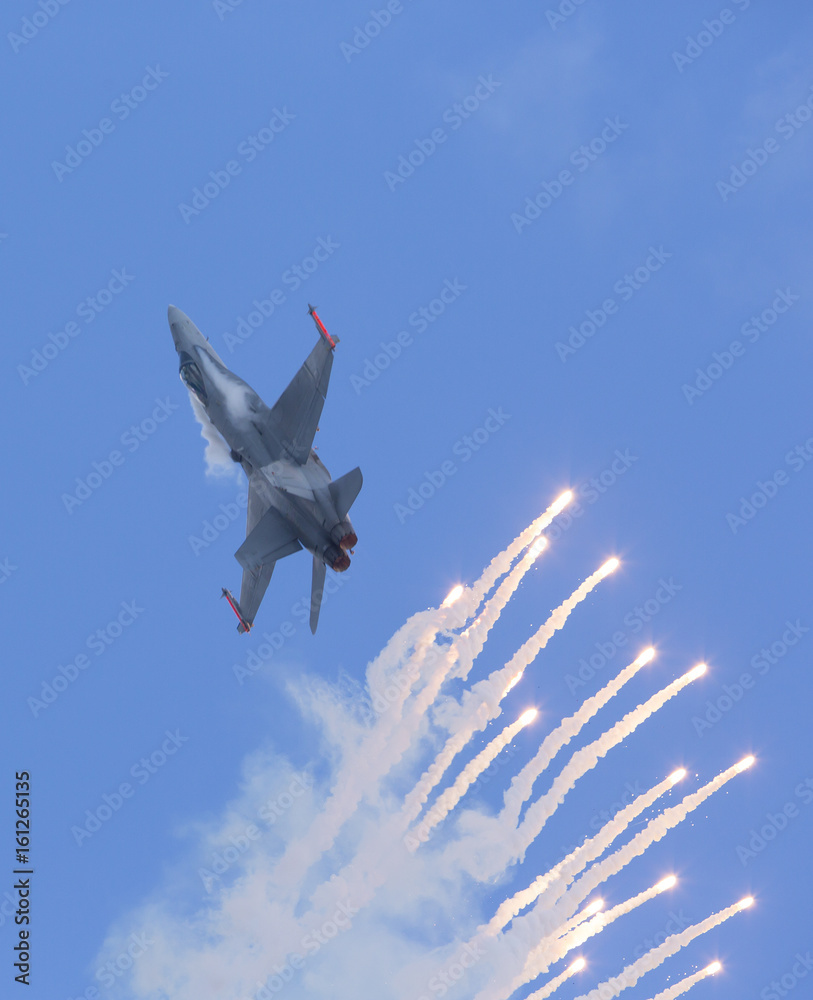 Modern jet fighter is firing a set of flares against a blue sky. Cloud ...