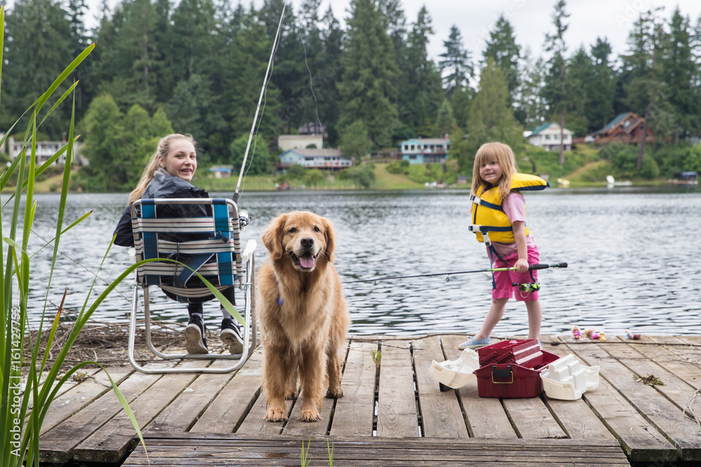 Two kids sitting on a dock fishing with a golden retriever dog Stock ...
