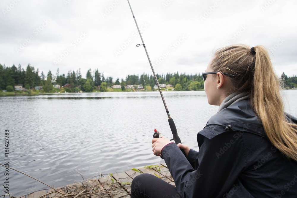 Teenage girl fishing in a lake while sitting on a dock Stock Photo ...