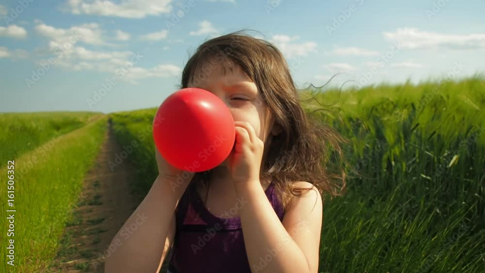 A child inflates a balloon. Little girl puffs up a balloon in nature ...