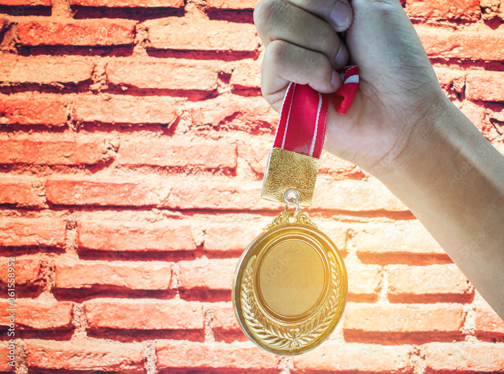 hand raised and holding gold medals on brick wall background, winner ...