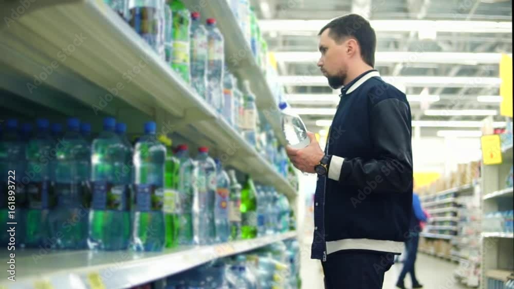 Man customer in the supermarket taking two bottles of mineral water and ...