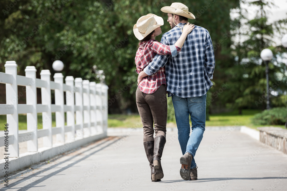 back view of cowboy with his girlfriend walking on pathway in park at ...