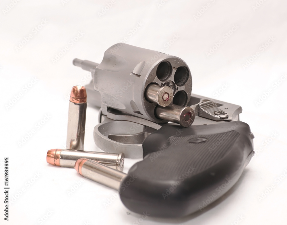 A semi loaded stainless revolver with several bullets next to the gun ...
