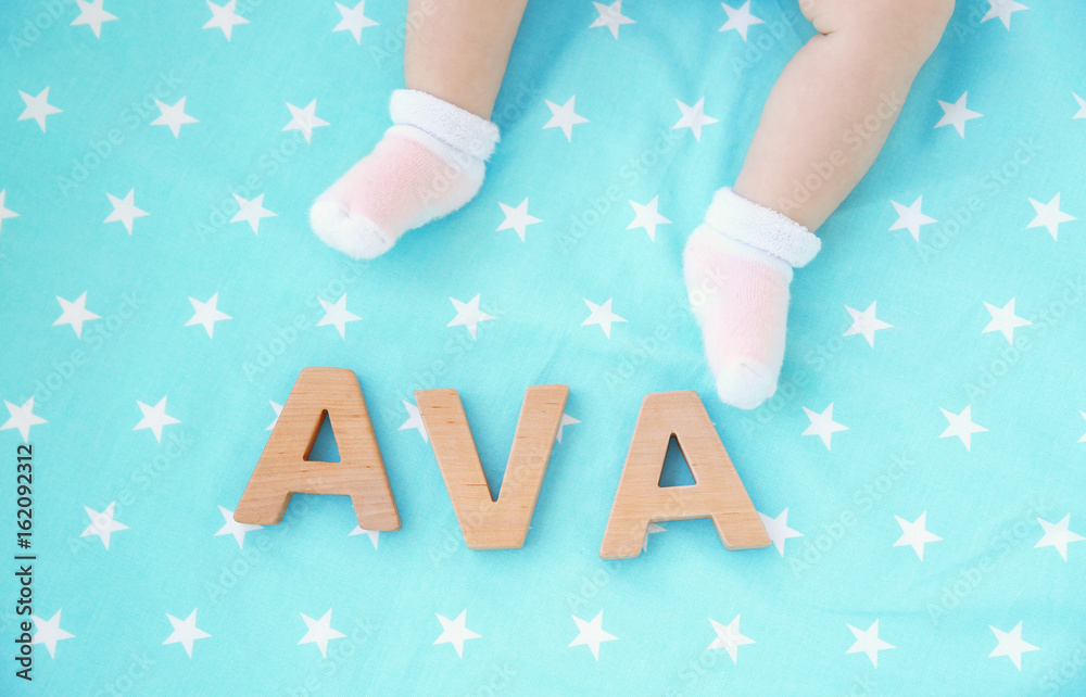 Legs of cute baby and word AVA composed of wooden letters on bed ...