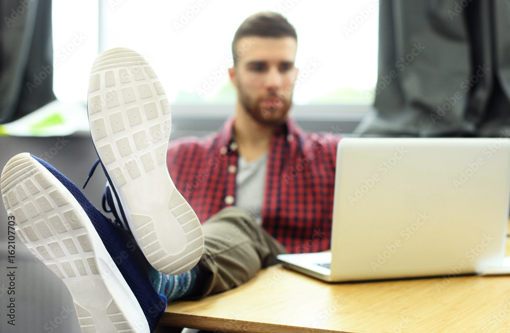 Portrait of a very relaxed young designer leaning back on his desk and ...