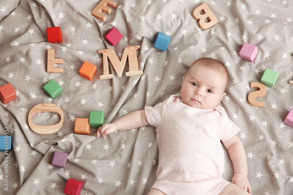 Cute baby with different letters and cubes lying on bed. Choosing name ...