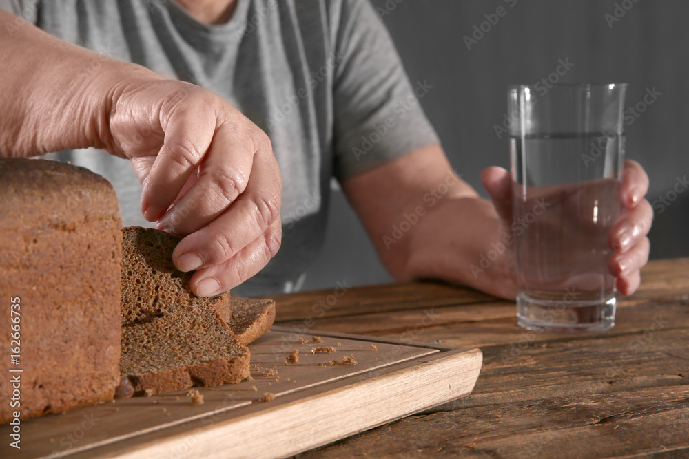 Elderly woman pinching off a piece of bread at table. Poverty concept ...