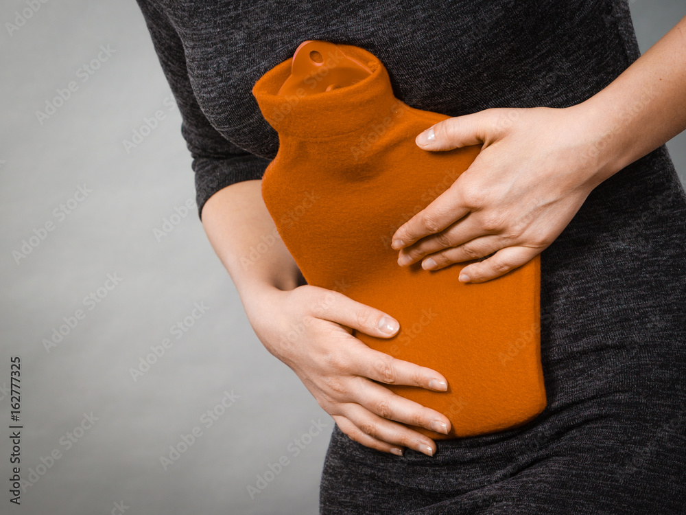 Girl having stomach ache, holding hot water bottle Stock Photo | Adobe ...