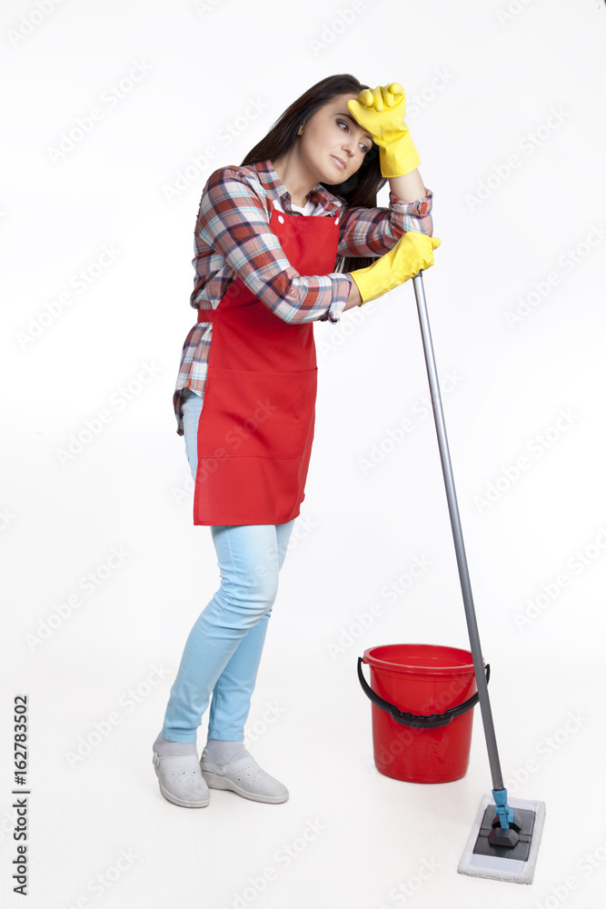 Sad and tired young woman in an apron, she leaned against the mop ...