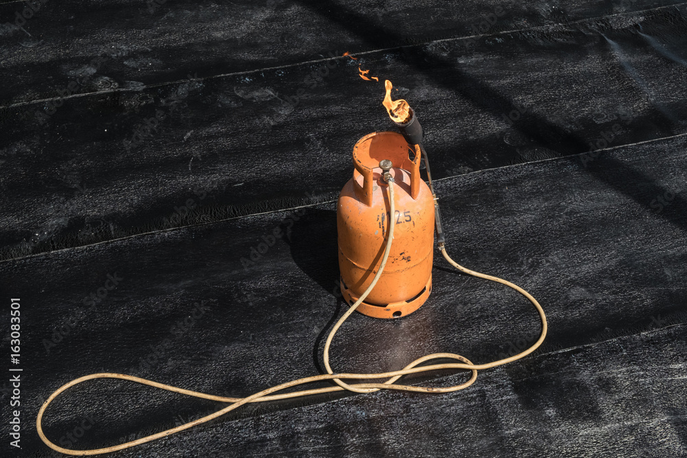 Orange butane gas tank with flame torch on the floor with bituminous ...