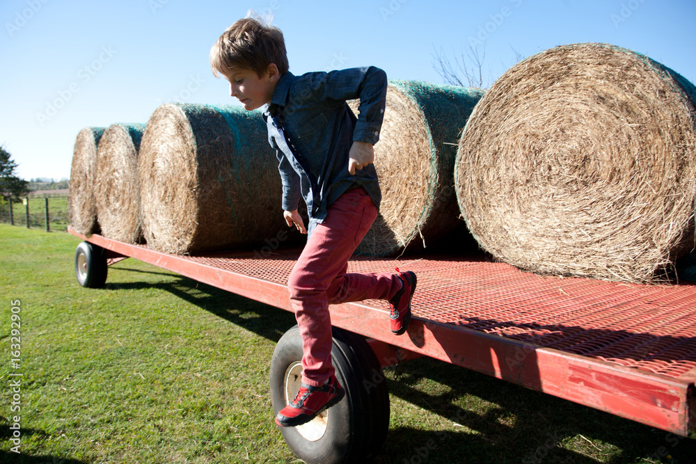 Boy jumping off the side of a farm tractor trailer with bales of hay ...