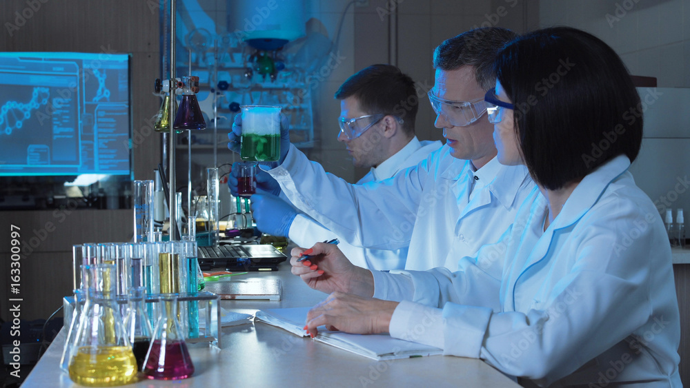Side view of three chemical scientists in protective suits using ...