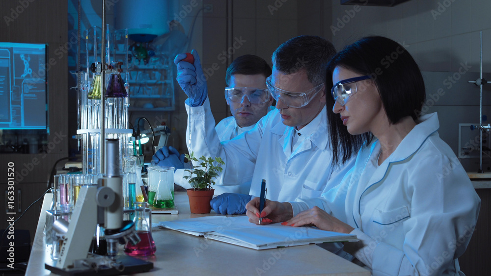 Side view of three chemical scientists in protective suits using ...