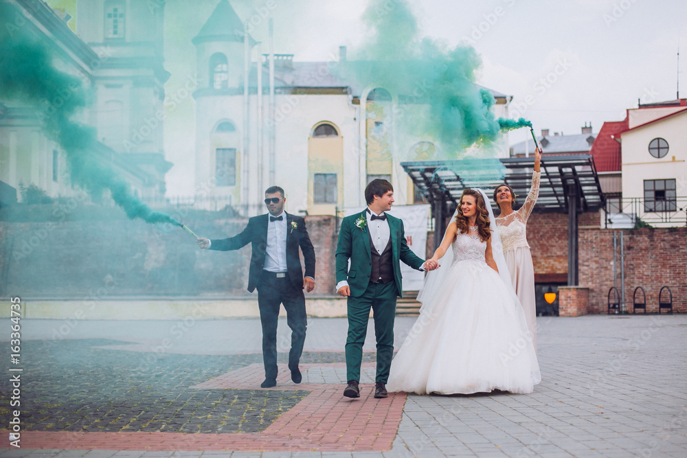 Newlyweds and their friends raise their hands with colors smoke ...