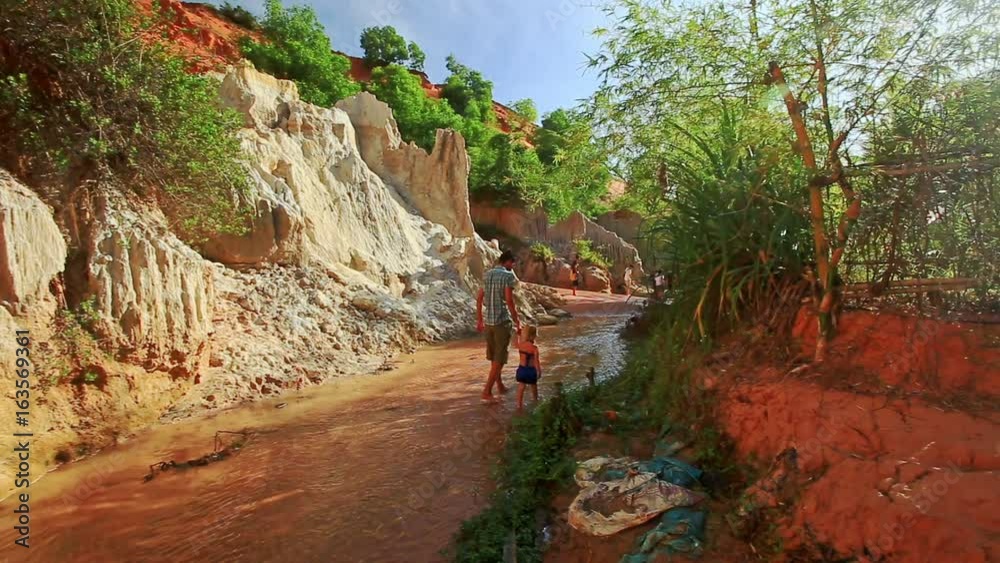 Dad and little girl in blue swimsuit walk in shallow stream water ...