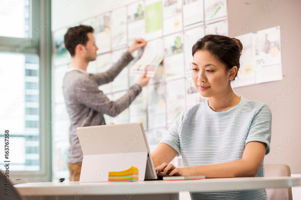 Female digital designer typing on laptop and colleague arranging mood ...