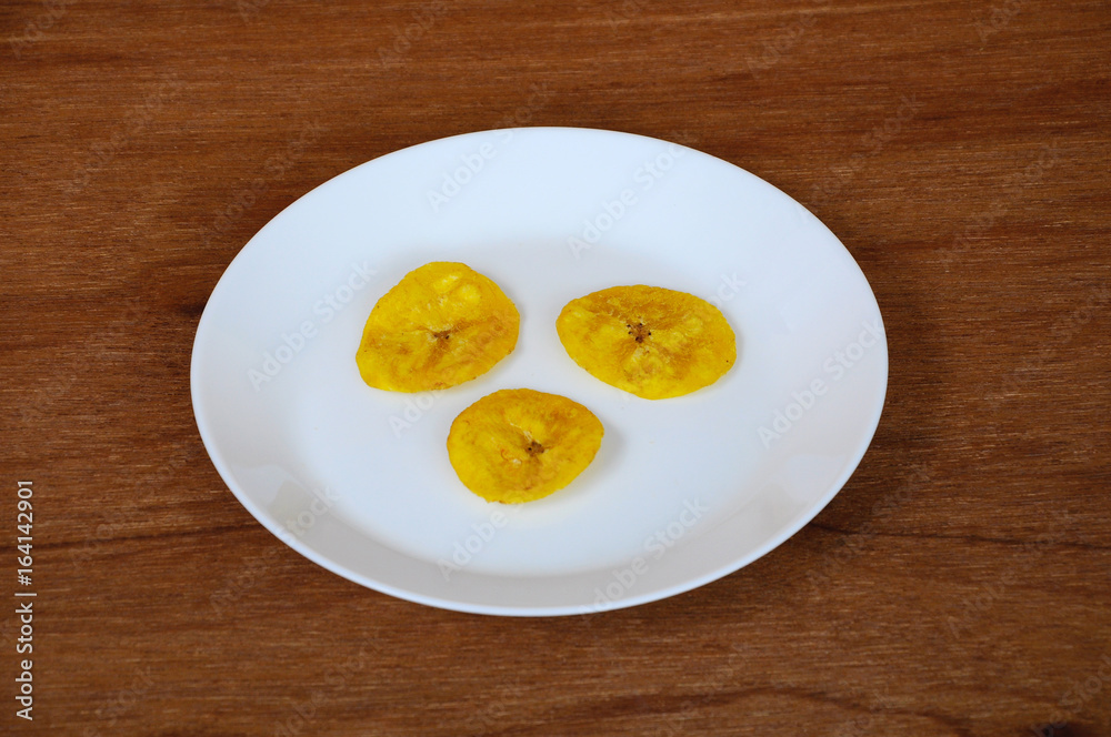 Dried and fried banana slices place on white plate isolated on wood ...