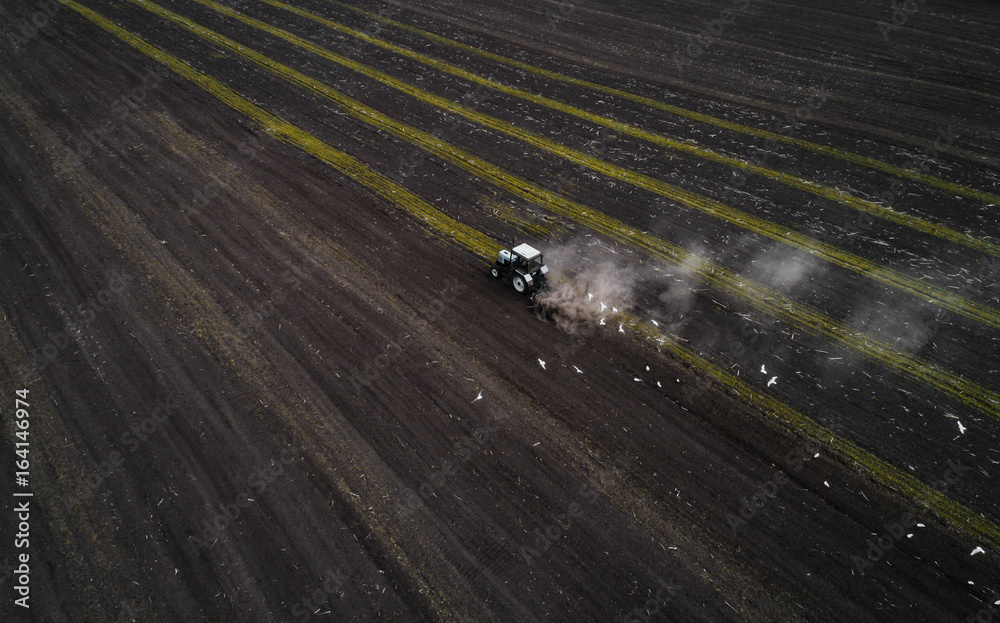 The white tractor plows the field against the backdrop of the black ...