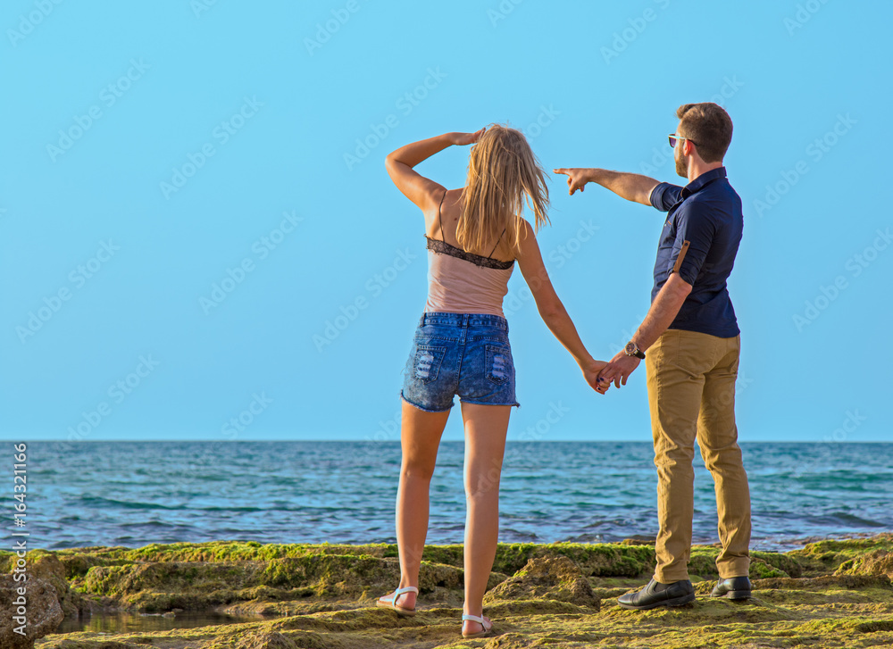 Young couple holding hands ,looking and pointing into the distance at ...
