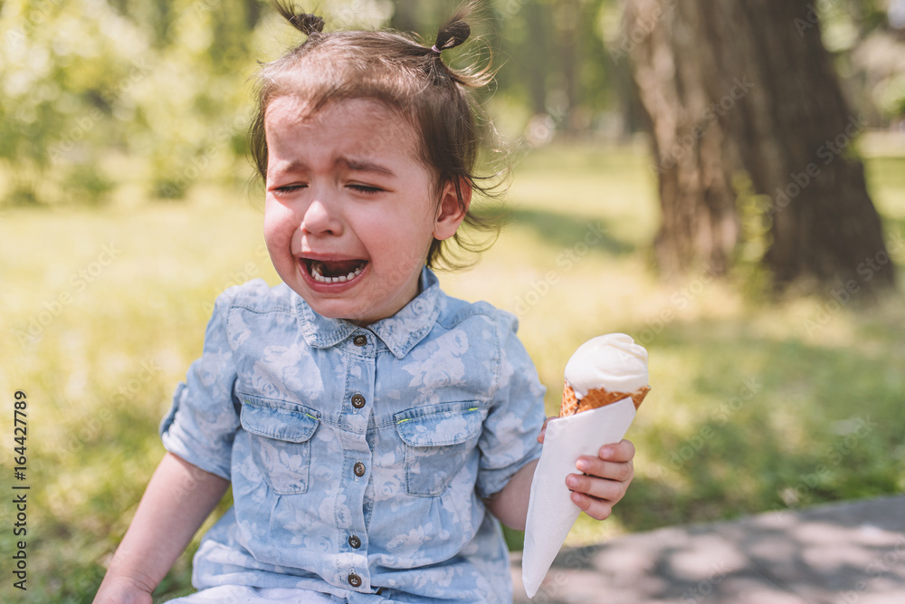 Portrait of sad kid crying with ice-cream cone in hand in the park ...