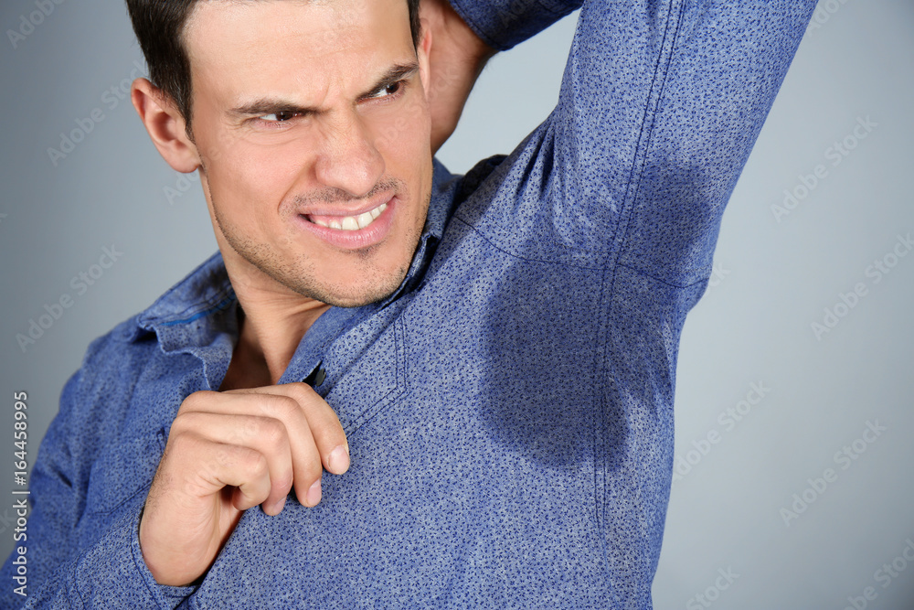 Handsome young man with wet spot on clothes under armpit against grey ...