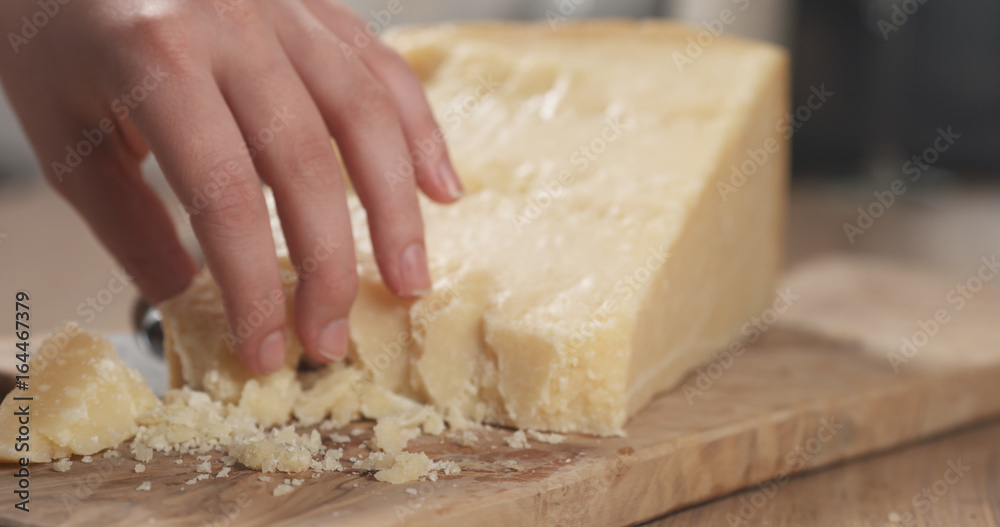 female hand taking pieces of hard parmesan cheese from olive board ...