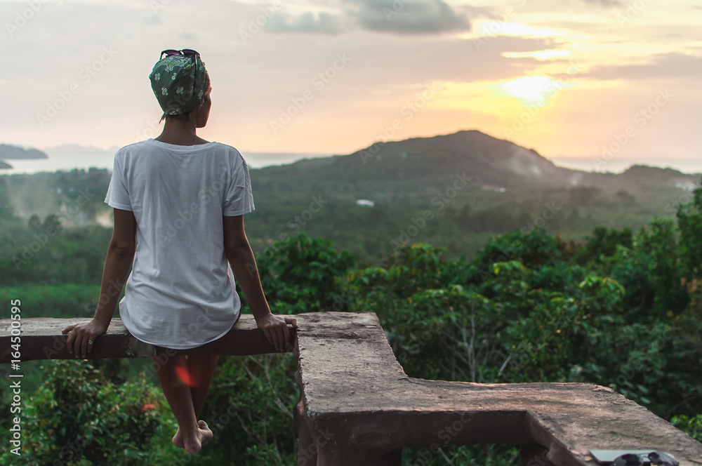The view from the back of a woman sitting on a high and watching sunset ...