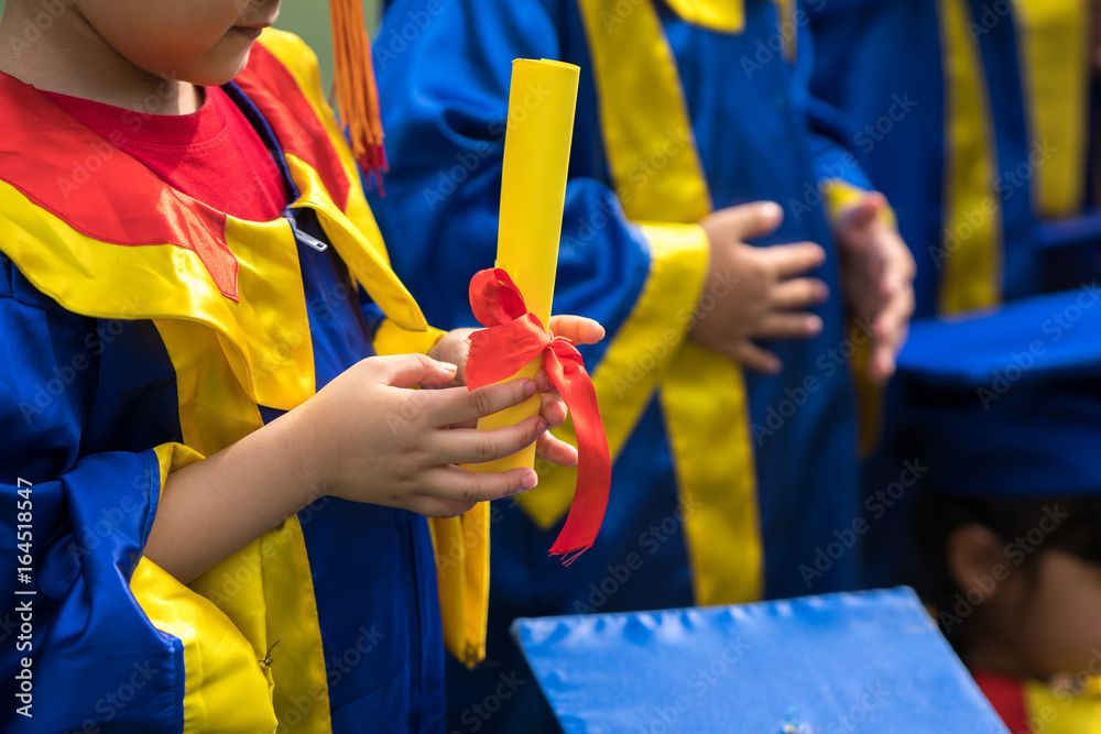 Preschool kid wearing graduation dress and holding diploma closeup ...
