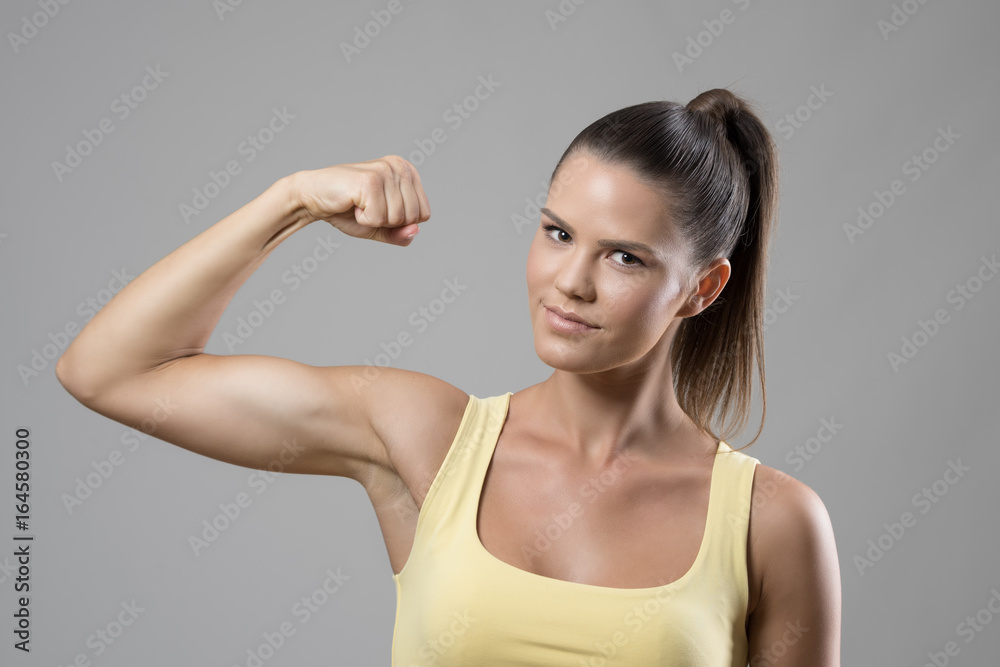 Young fit sporty woman in singlet with ponytail flexing biceps arm ...