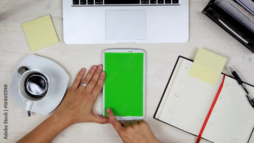 woman using a mobile phone / tablet PC with green screen at her desk in ...