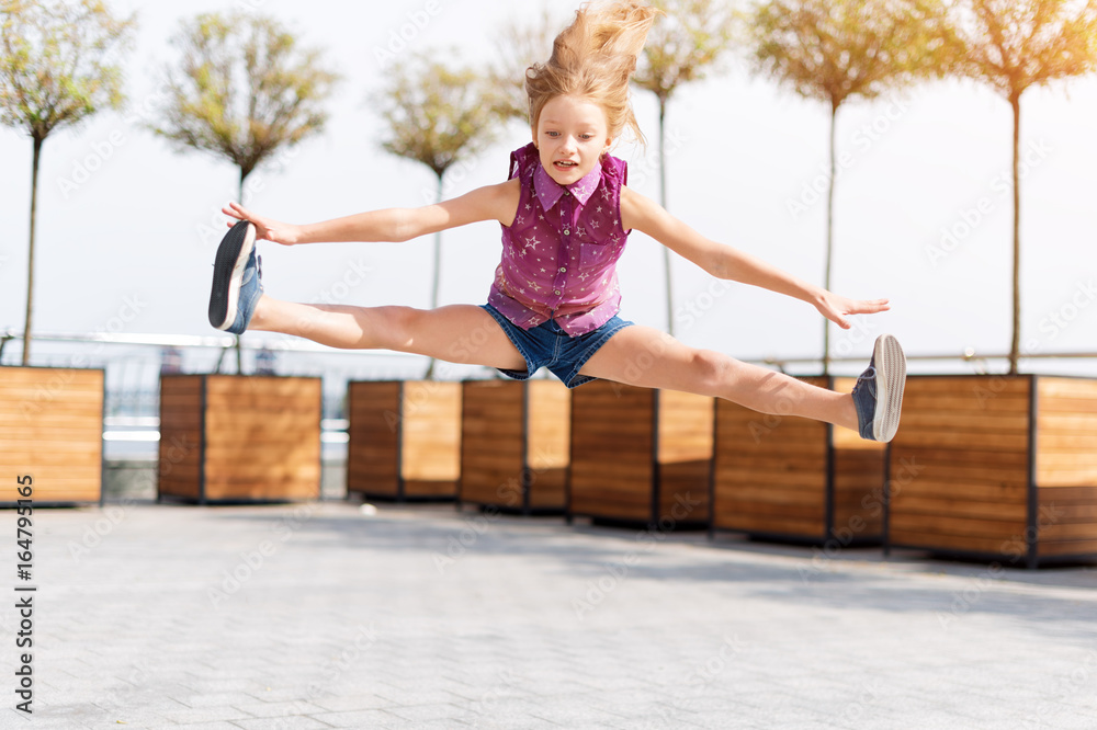 Active kid girl gymnast jumping on the street, doing splits. Stretching ...