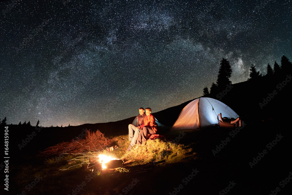 Night camping. Romantic couple tourists have a rest at a campfire near ...