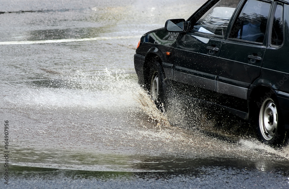 Car splashes through a large puddle on a flooded street. Motion car ...