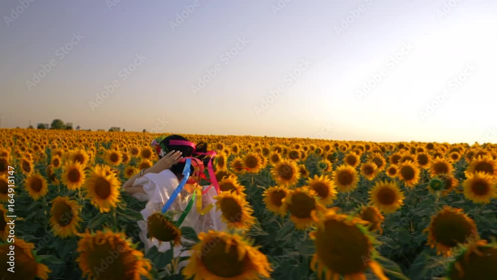 Beautiful girl with wreath running on yellow sunflower field, raising ...