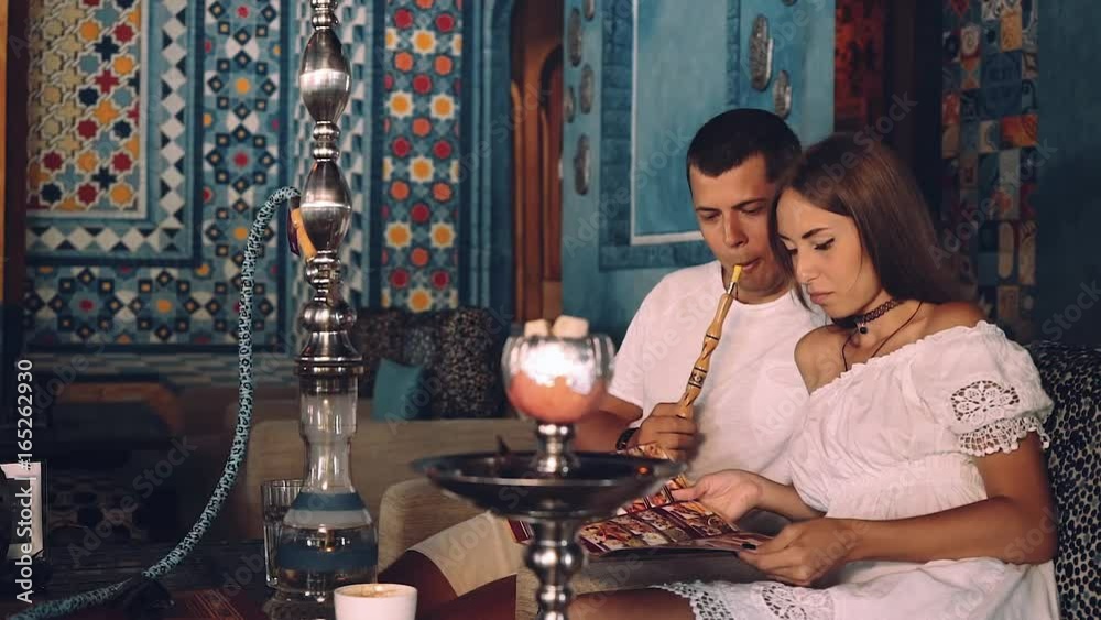 Young couple sitting on a couch in shisha cafe, arabic style, smoking ...