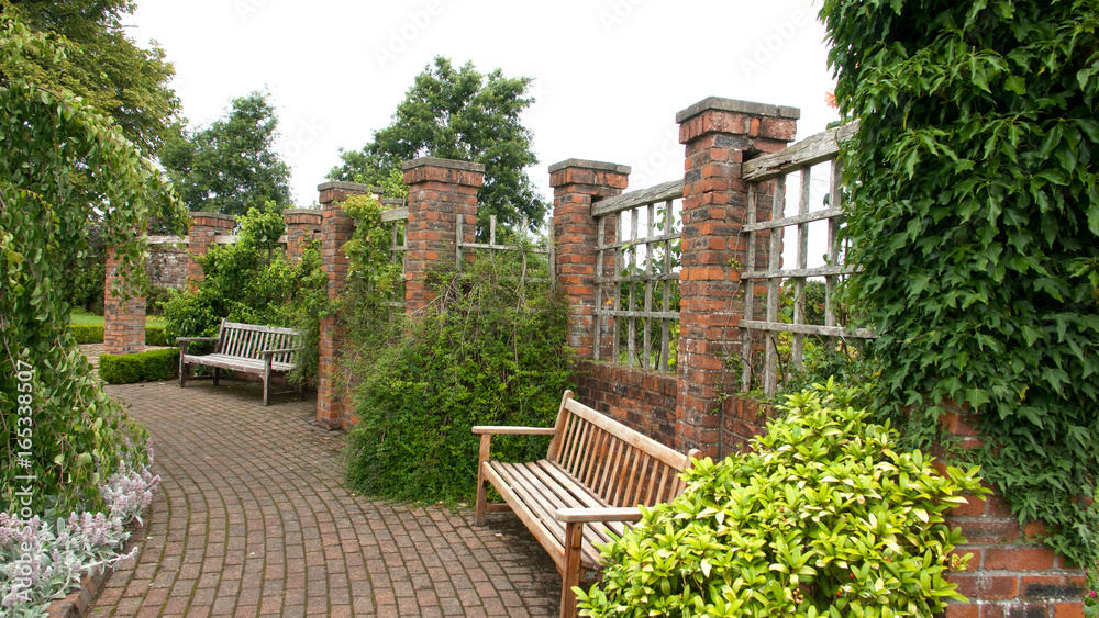 Benches in a walled garden with monoblock path and red brick pillars ...