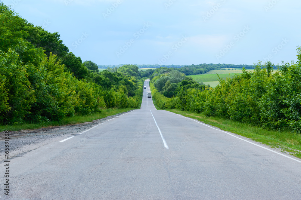Asphalt road, goes into the distance. Green trees are on both sides ...