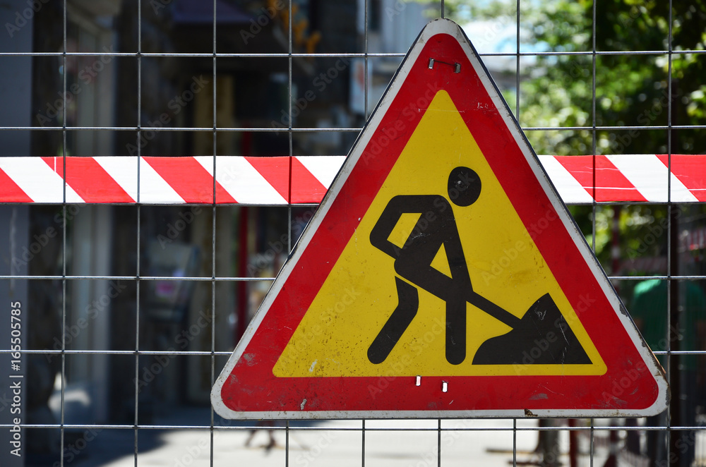 The warning sign "under construction" is attached to a metal mesh fence ...