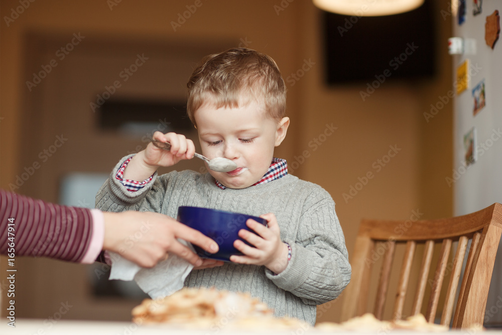 Kid eating using blue bowl and spoon. Mother's hands holding a bowl ...