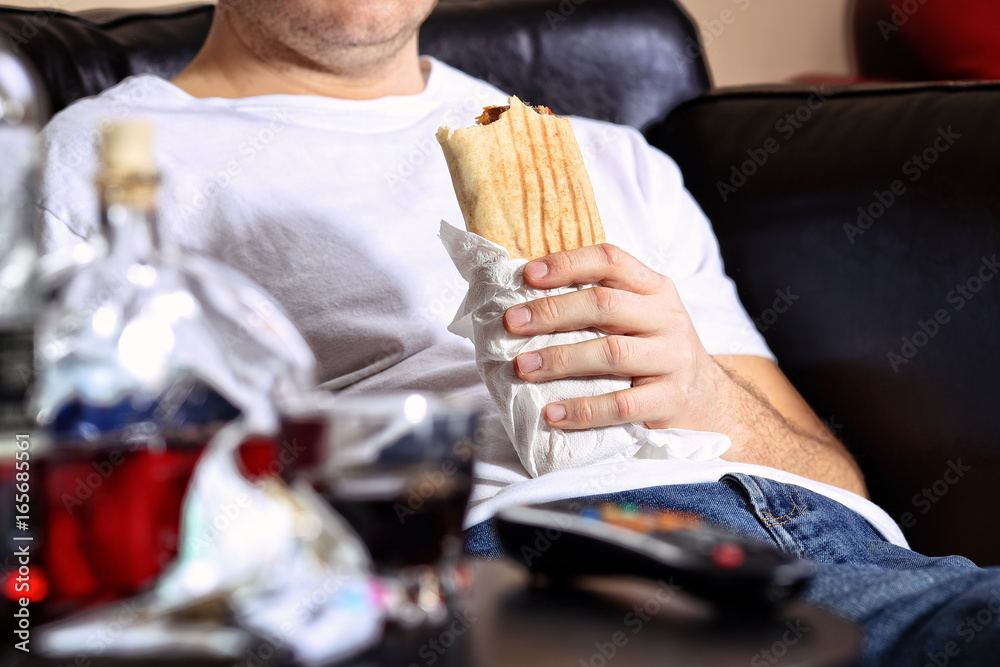 Lazy and fat man eats a kebab on the couch Stock Photo | Adobe Stock