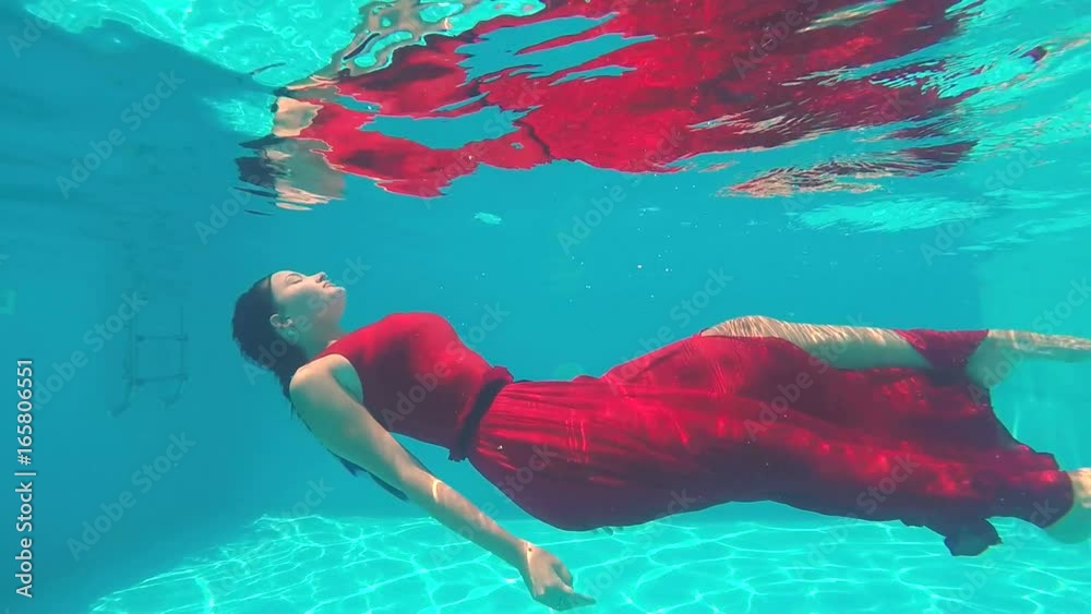 Young girl with braids in long red dress swims under water in swimming ...