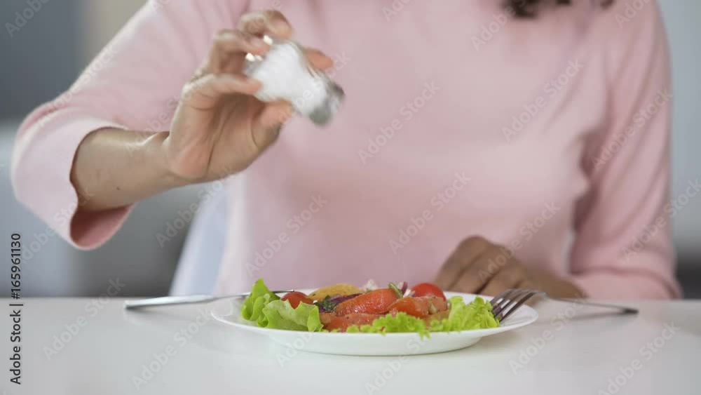 Woman adding too much salt to her food, unhealthy eating, dehydration ...