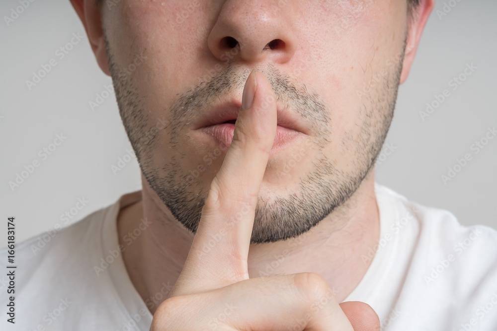 Foto de Young man has finger on lips and showing be quiet gesture. do ...